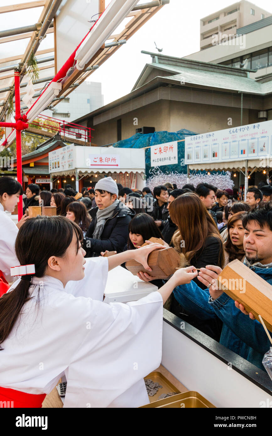 Japanese new year, shogatsu. Shrine Maidens, Miko, at busy counter selling Omikuji paper fortune ...