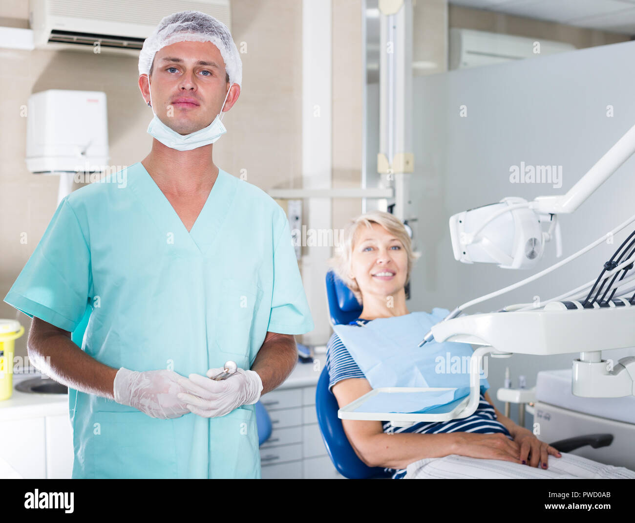 Confident male dentist standing in dental office with female patient in ...