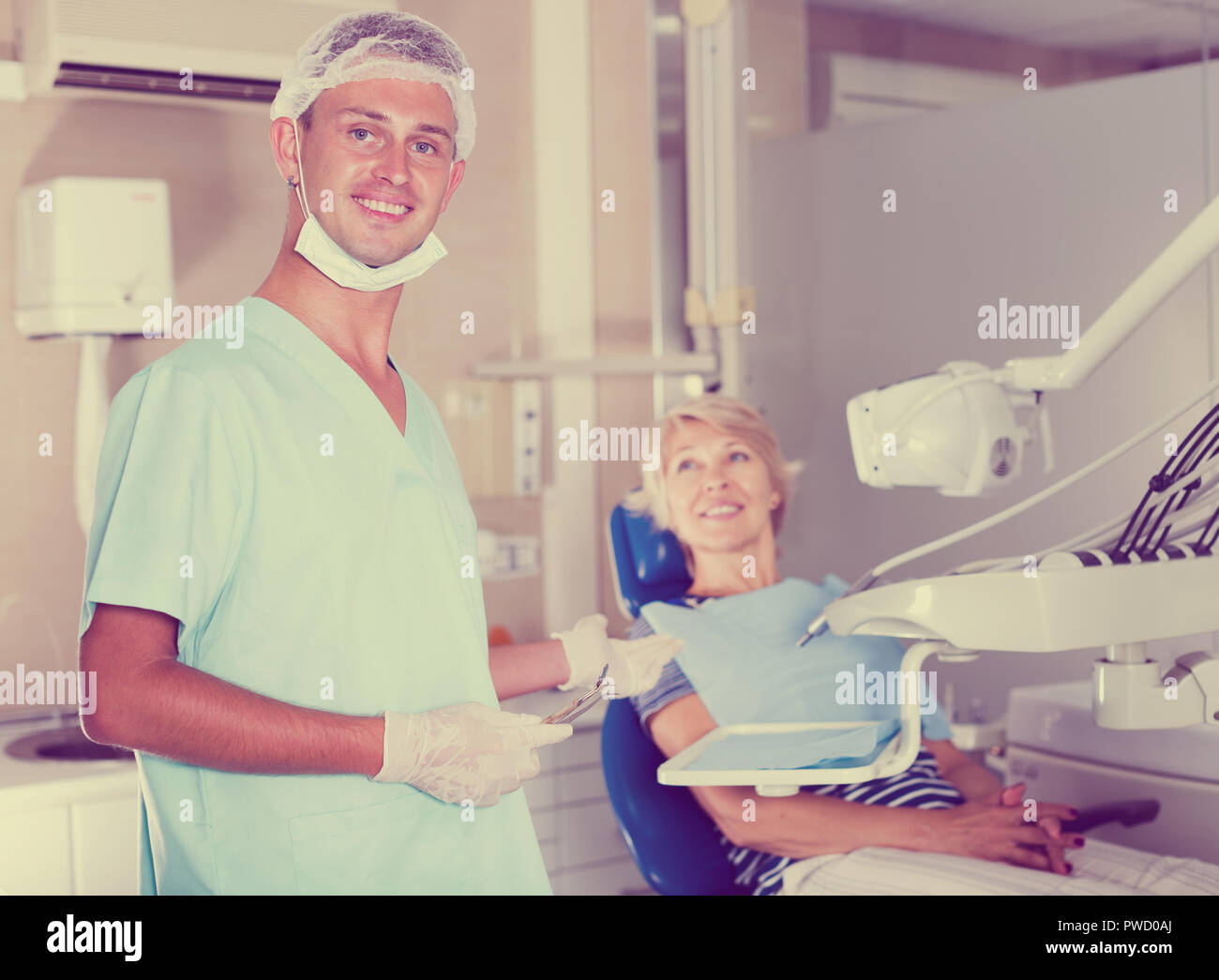 Portrait of professional dentist in dental clinic with patient behind ...