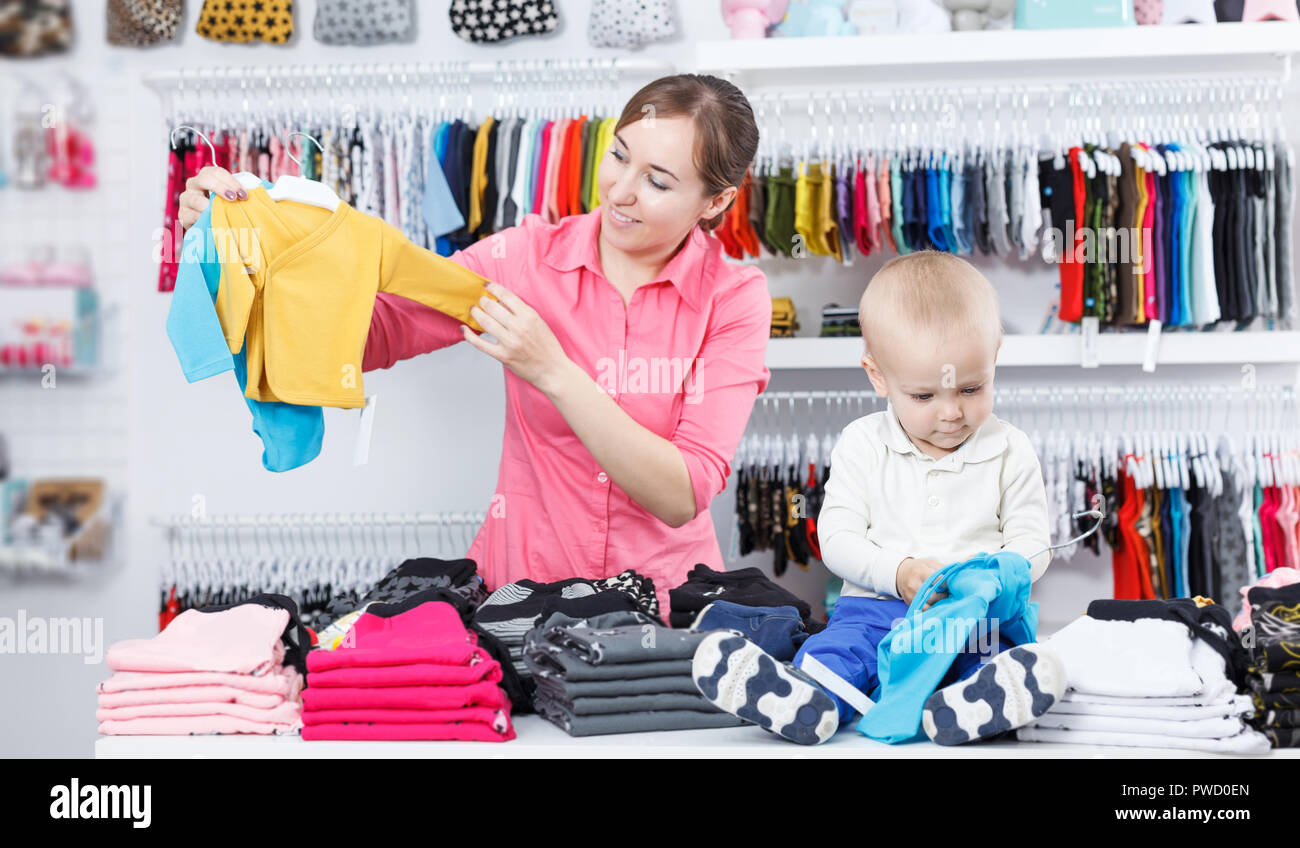 little positive kid who is posing when his mother choosing clothes in ...