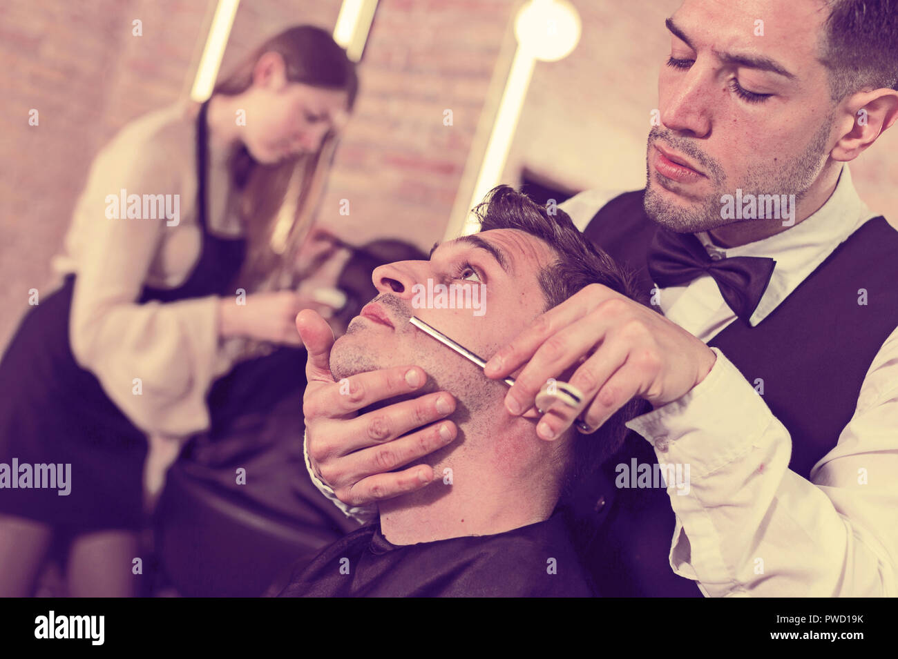 Male client getting old-fashioned shave with straight razor from male ...