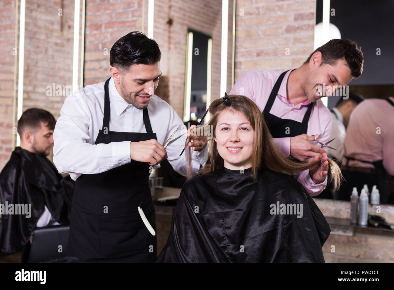 Attractive long-haired brunette getting haircutting from two ...
