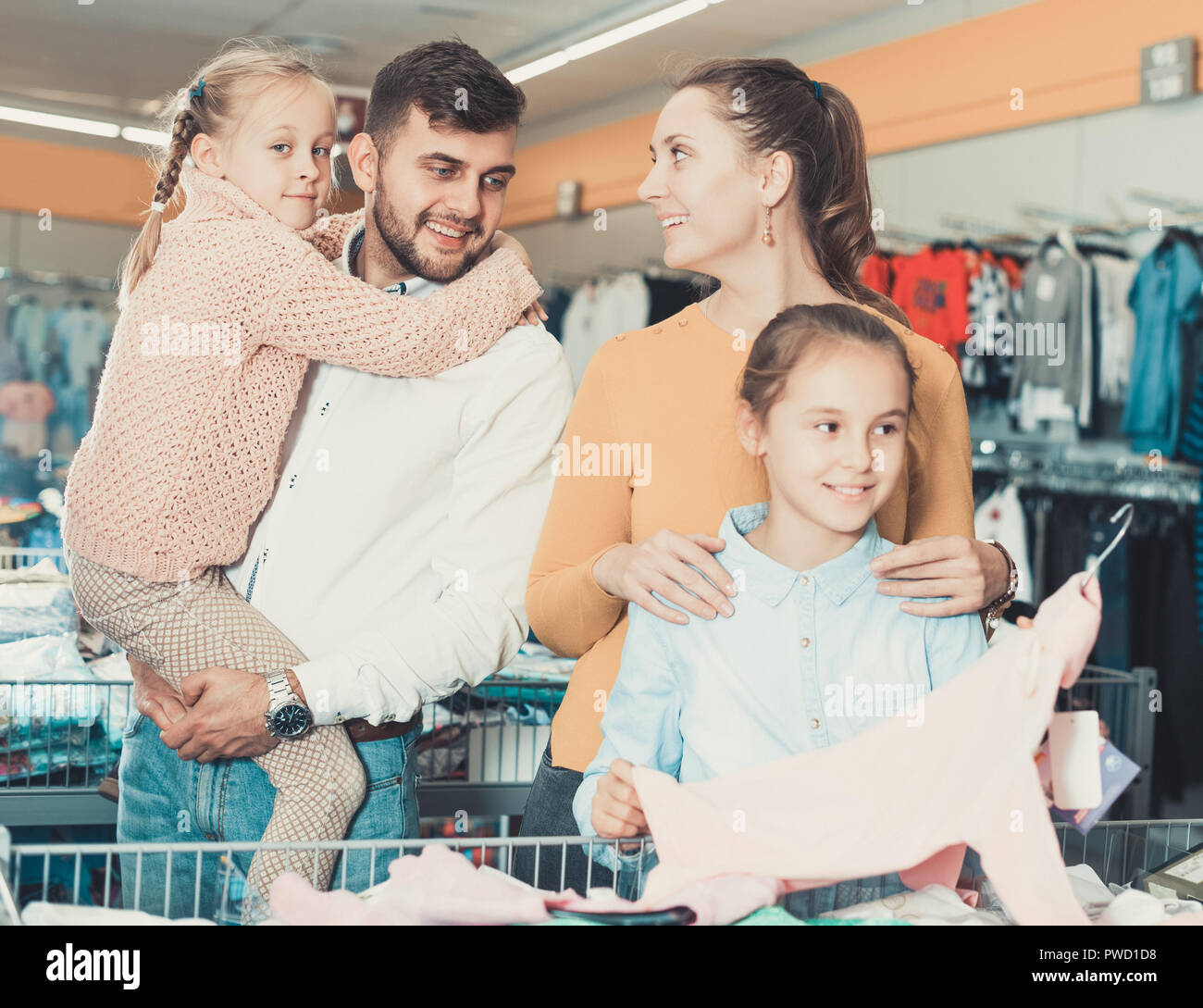 Happy young family with two girls choosing new clothes in mall Stock ...