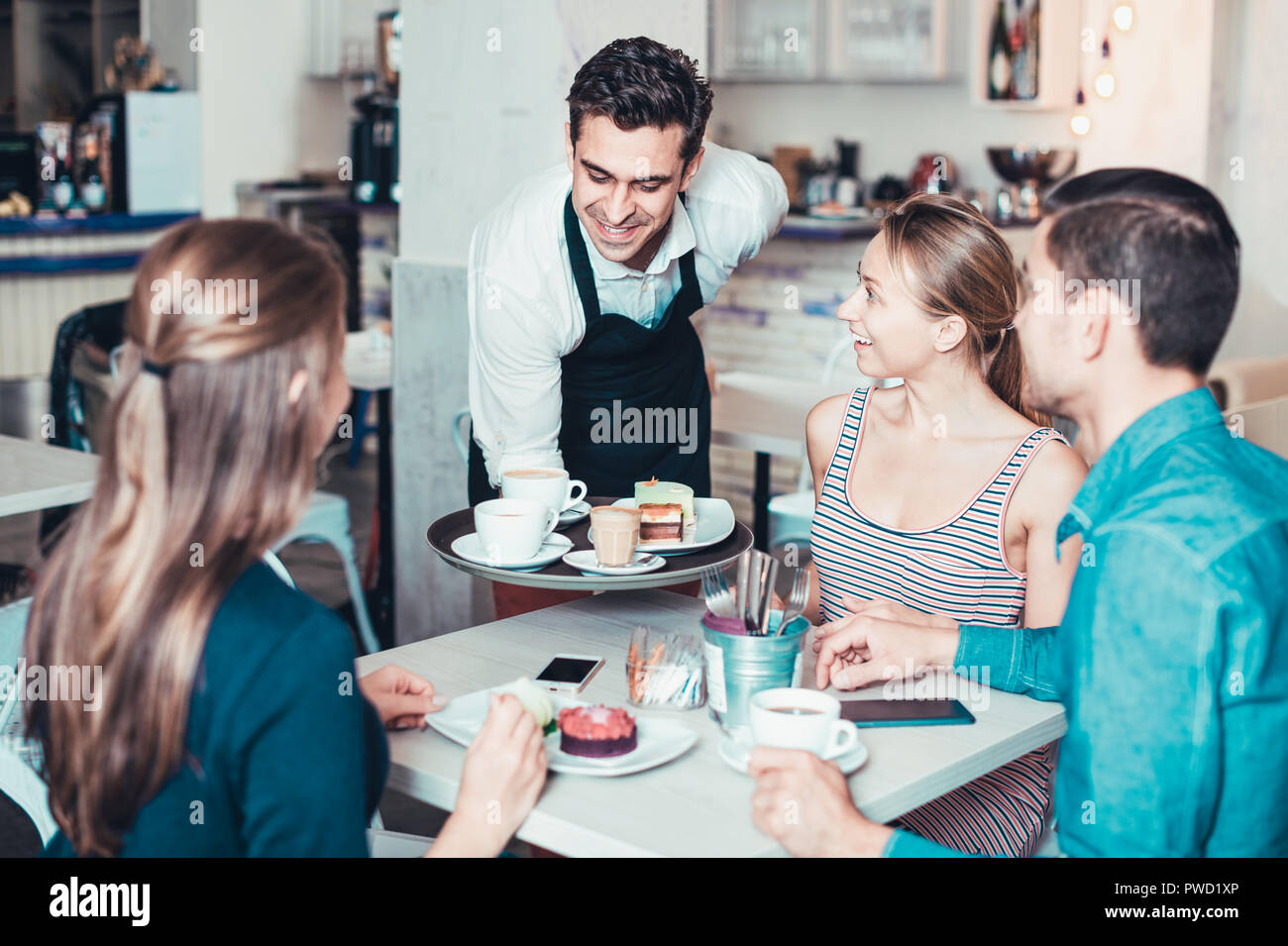 Smiling waiter showing hospitality and serving visitors in cozy ...