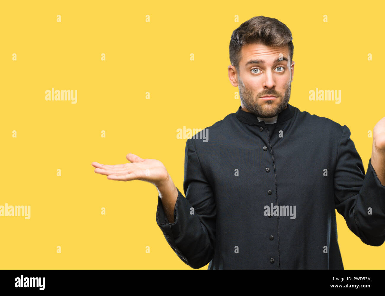 Young catholic christian priest man over isolated background clueless ...