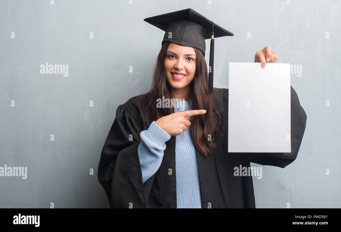 Young brunette woman over grunge grey wall wearing graduate uniform ...