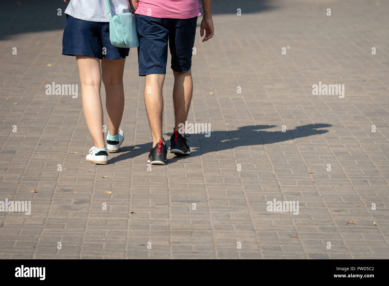 On a sunny day, a couple of people walk along the sidewalk. The human ...