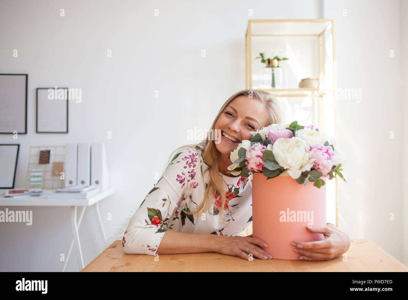 Happy blonde woman in a modern office with flowers in a hat box ...