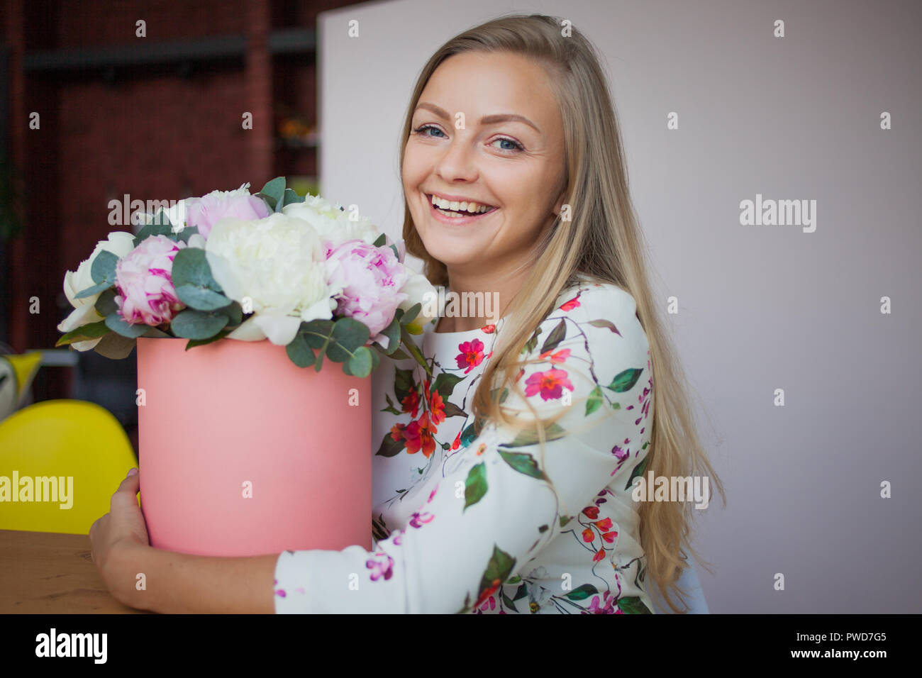 Happy blonde woman in a modern office with flowers in a hat box ...