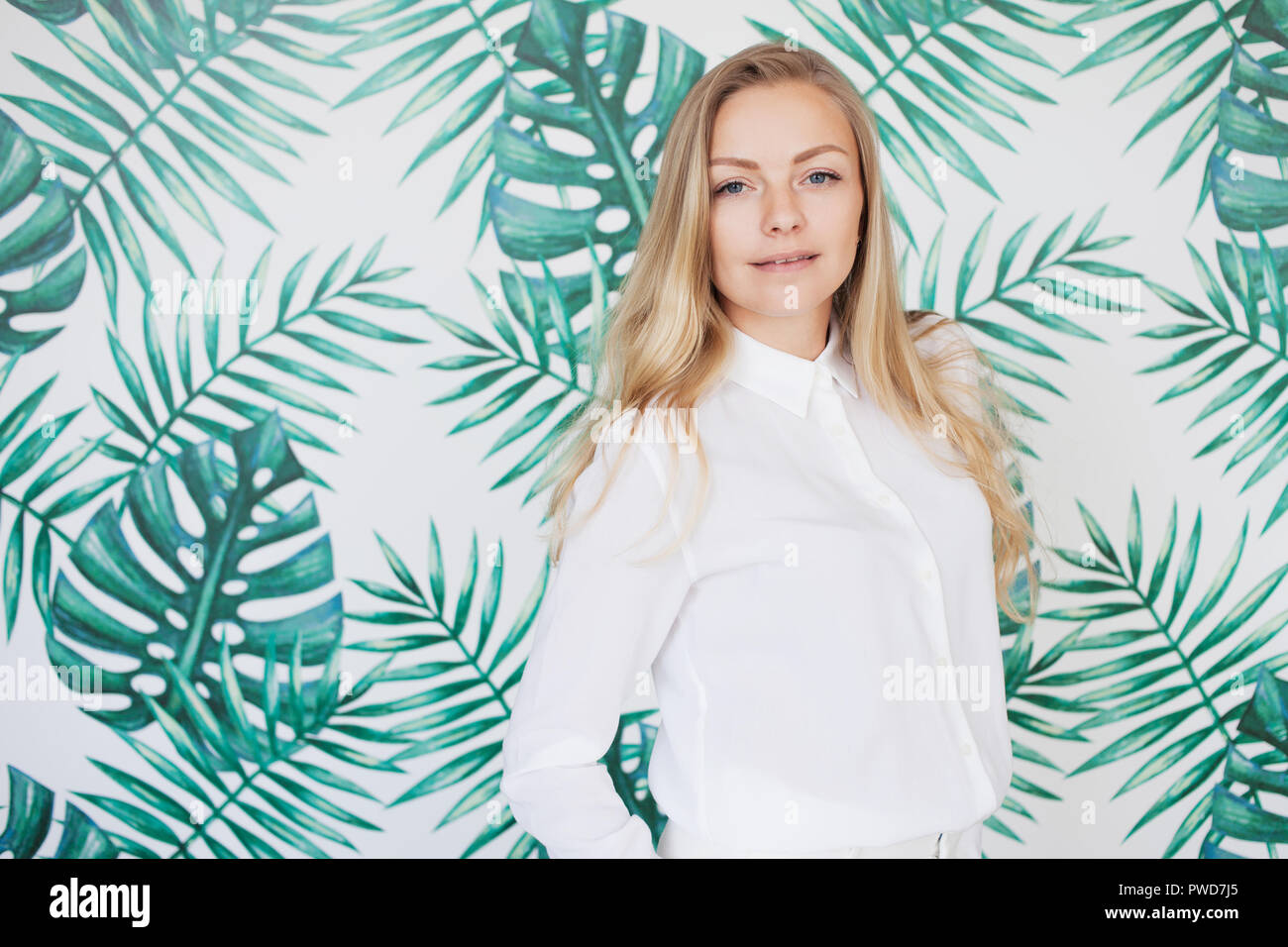 Cute young blonde woman in white shirt on wall background with pattern ...