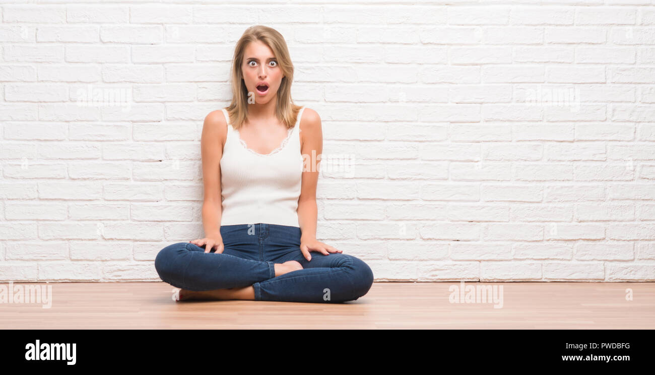 Beautiful young woman sitting on the floor at home afraid and shocked ...