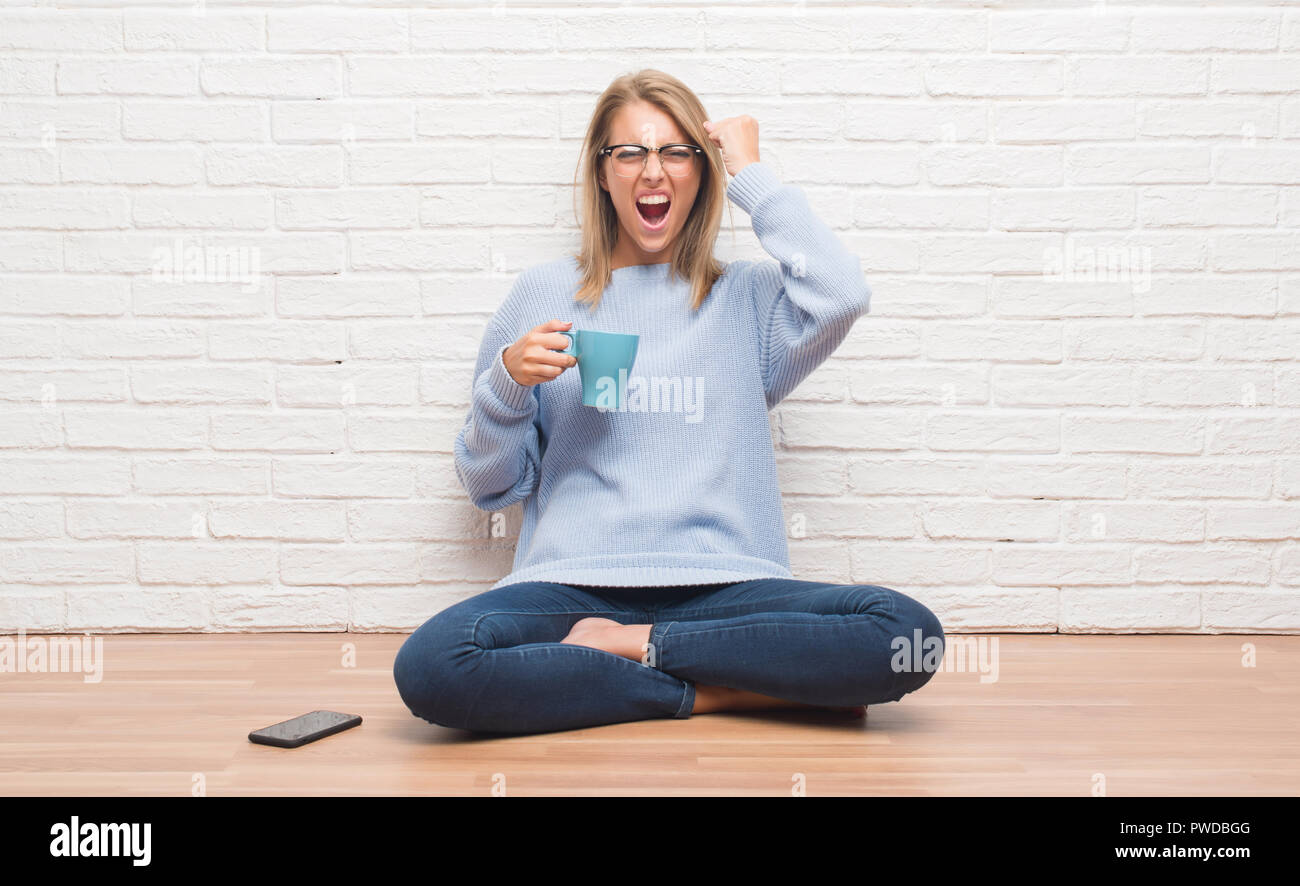 Beautiful young woman sitting on the floor driking cup of coffee at ...