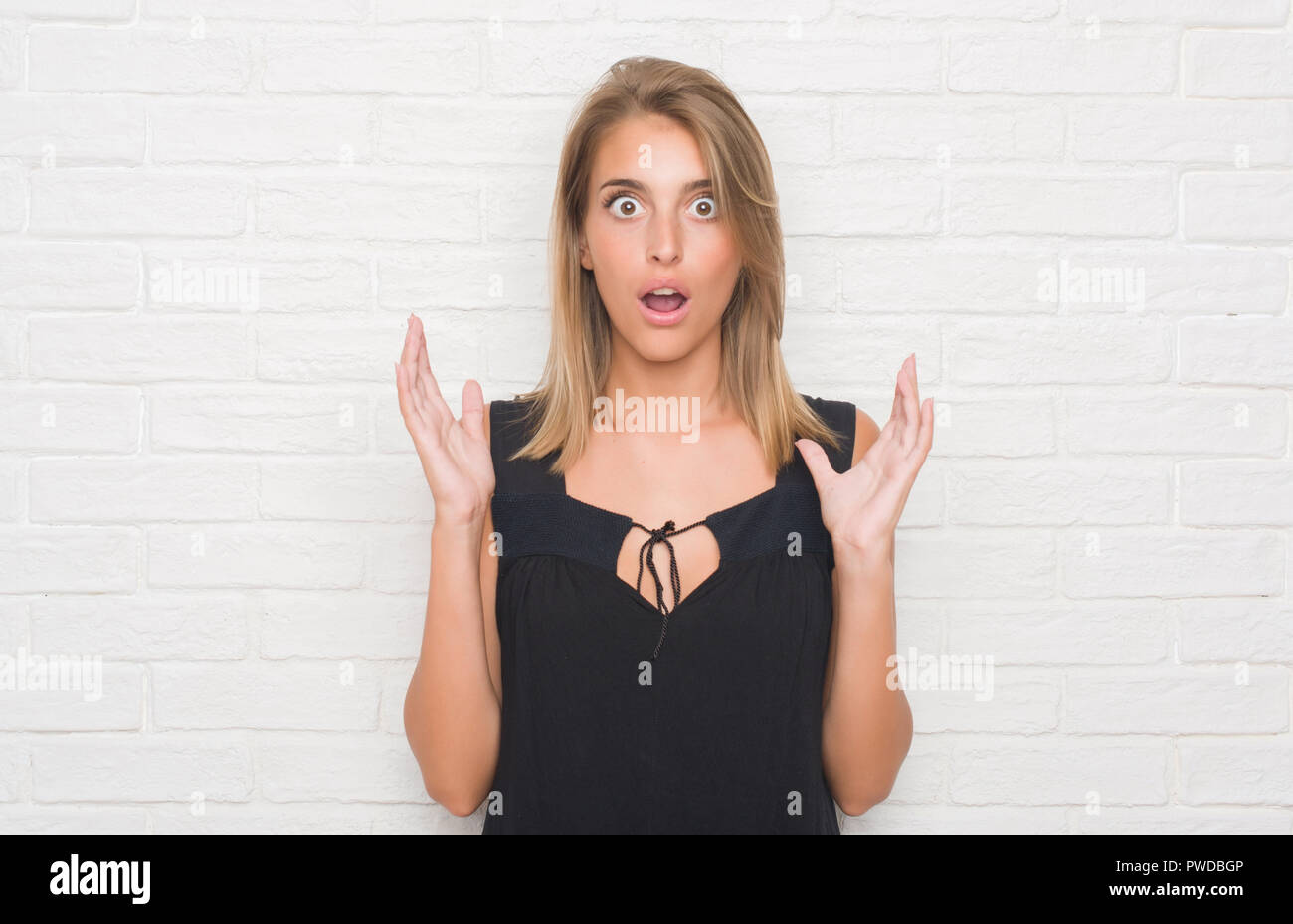 Beautiful young woman over white brick wall scared in shock with a ...