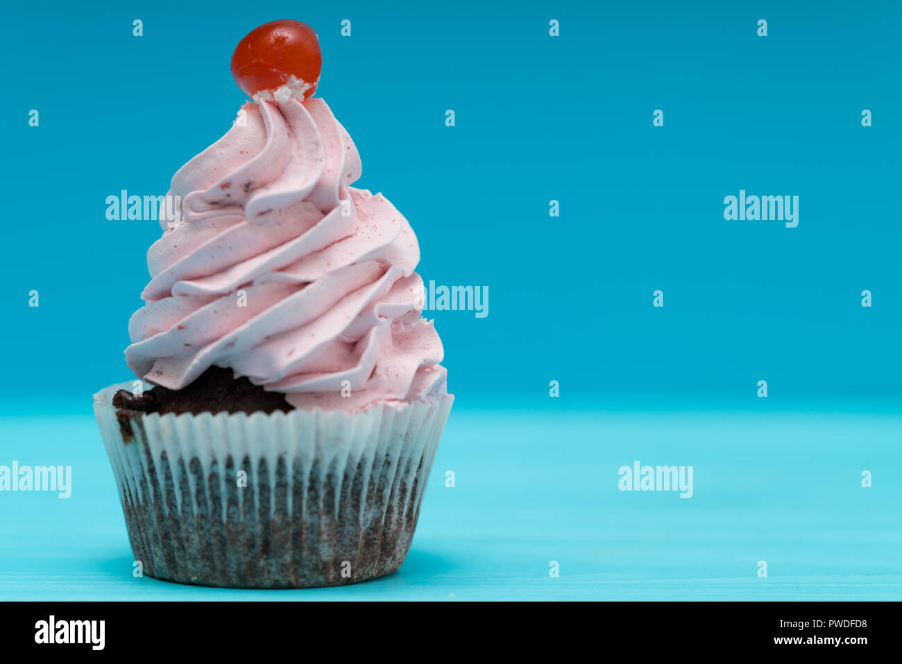 Single cupcake with twirled pink icing and cherry on a blue background ...