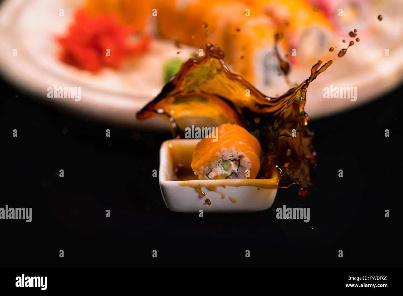 Fresh salmon sushi roll falling into a side dish of soy sauce with a ...