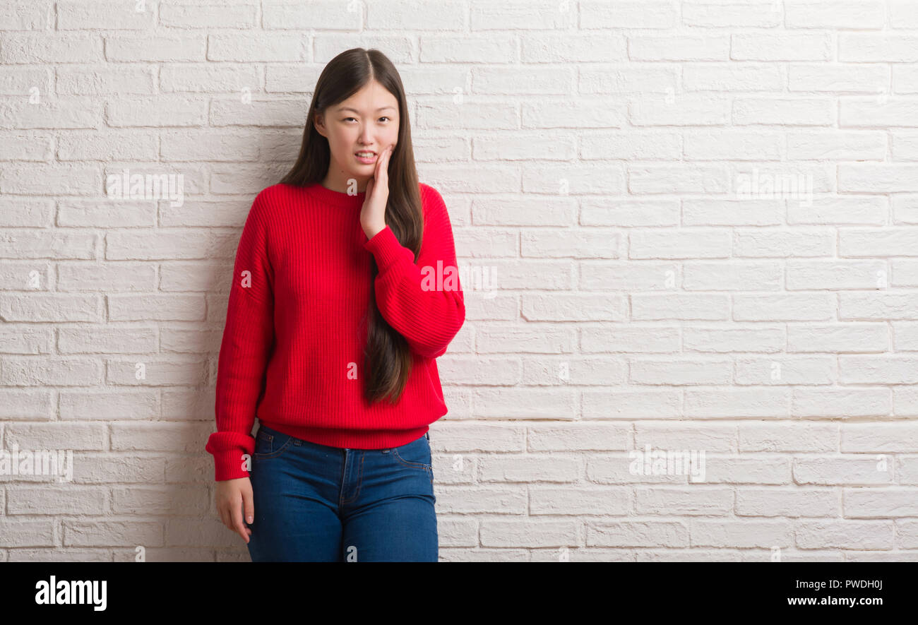Young Chinese woman over brick wall touching mouth with hand with ...