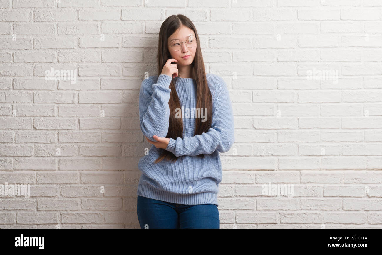 Young Chinise woman over white brick wall with hand on chin thinking ...