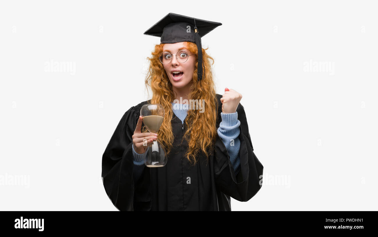 Young redhead student woman wearing graduated uniform holding hourglass ...