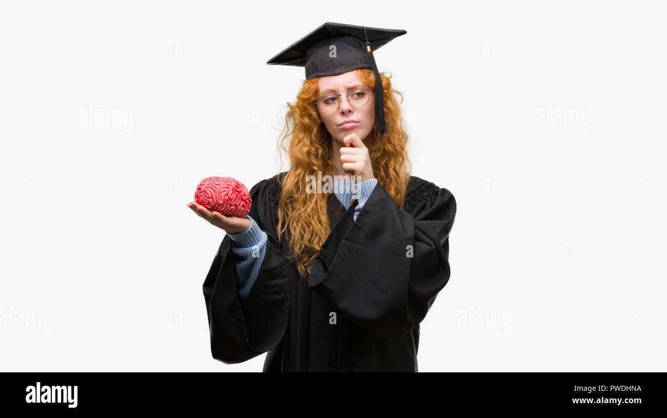 Young redhead student woman wearing graduated uniform holding brain ...