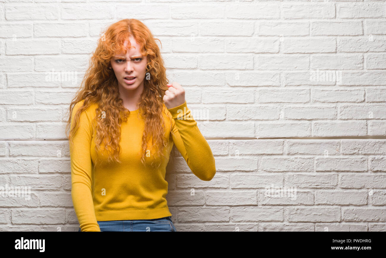Young redhead woman standing over brick wall annoyed and frustrated ...