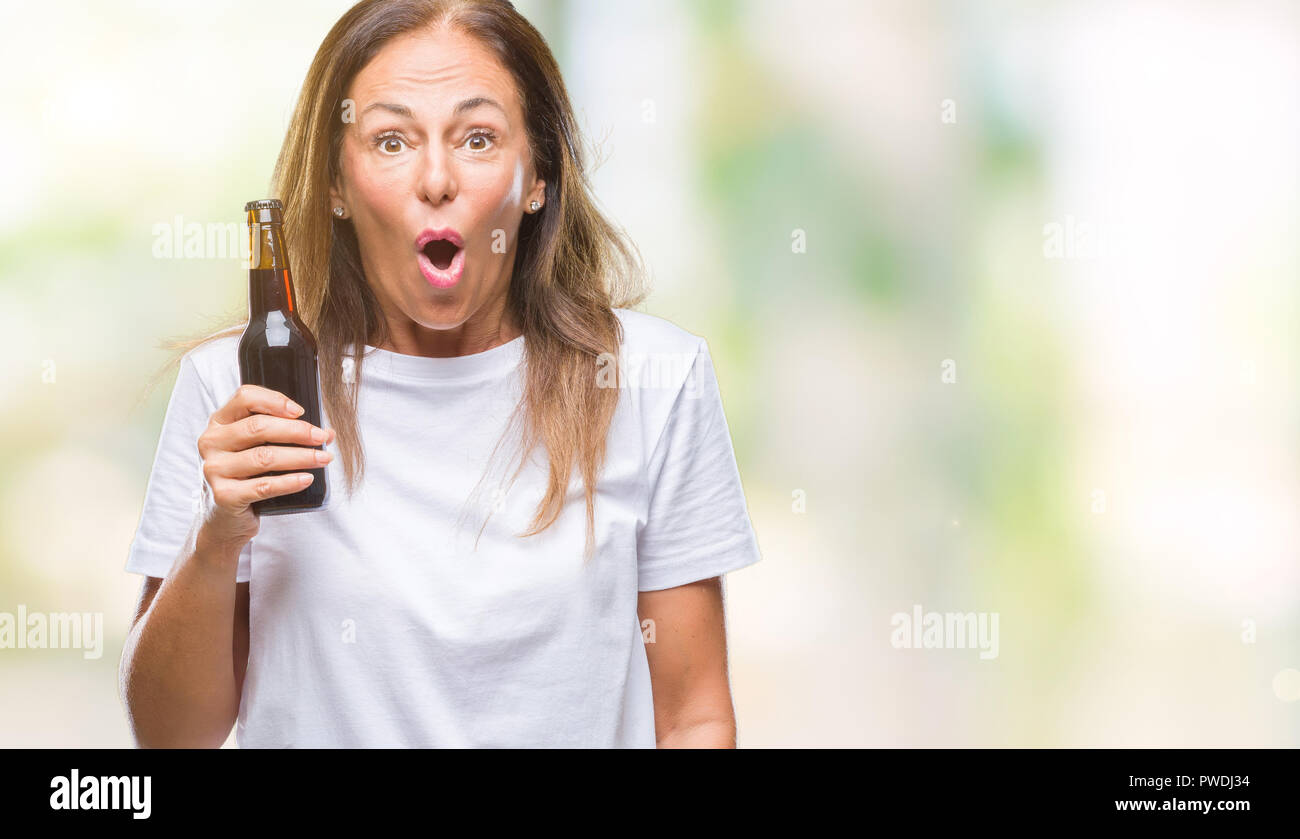 Middle age hispanic woman drinking beer over isolated background scared ...