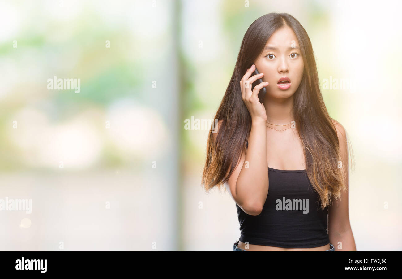 Young asian woman speaking on the phone over isolated background scared ...