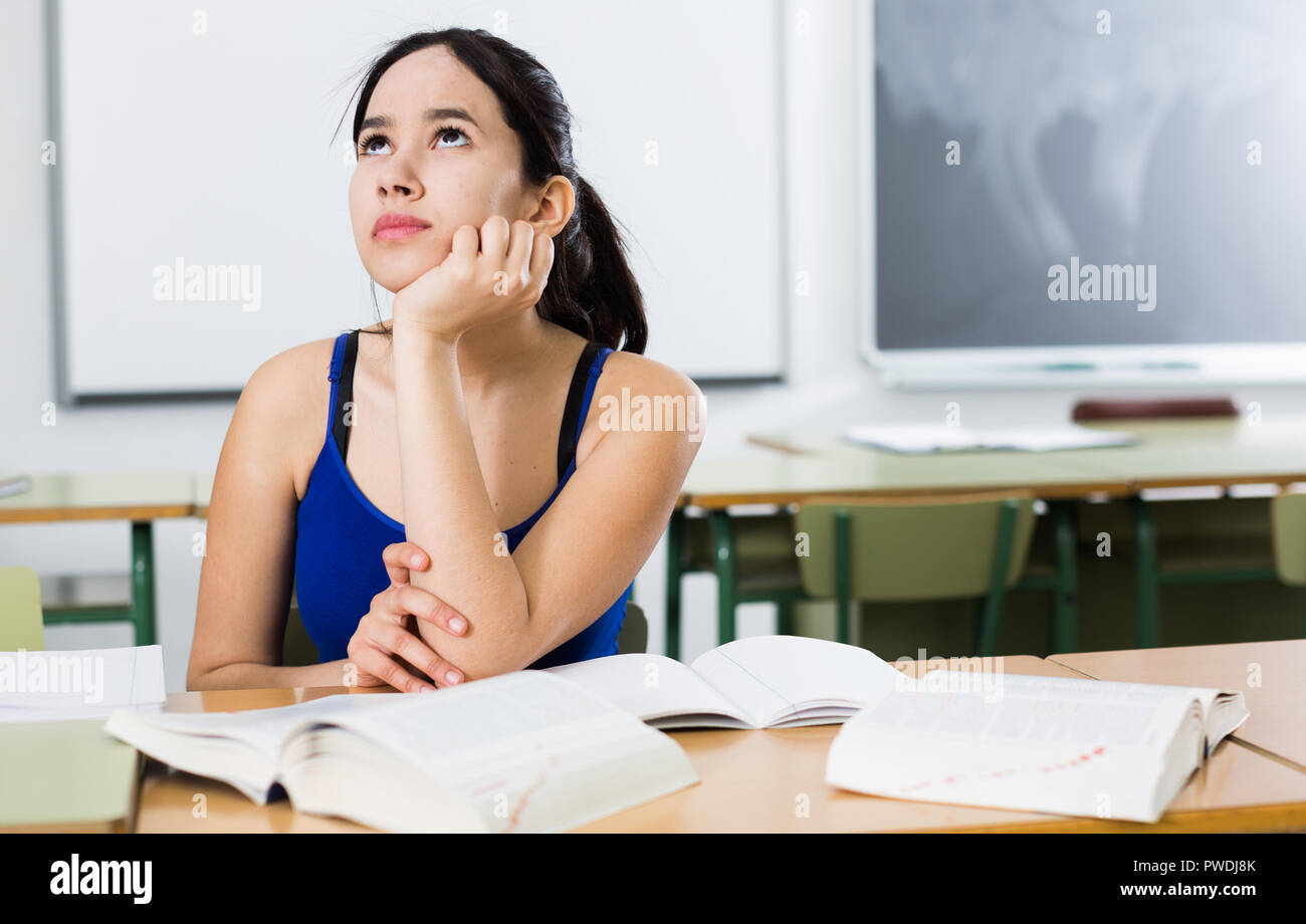 Young girl is thinking about difficult task at the desk in the class ...