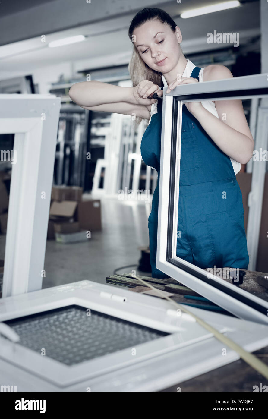 Diligent workwoman assembling PVC window in workshop with manual tools ...