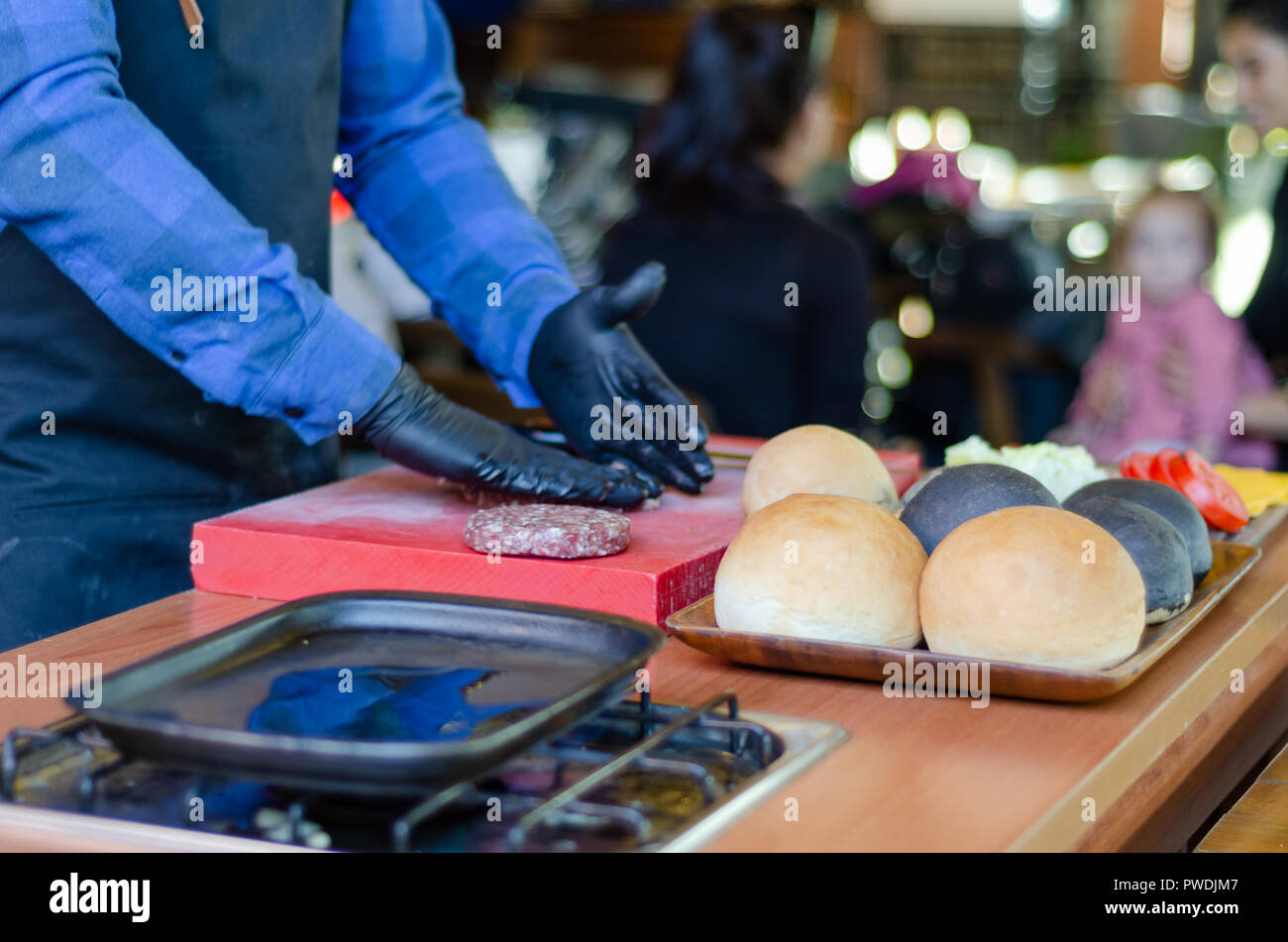 Chef is preparing a burger on the table in restaurant.He hands in black ...