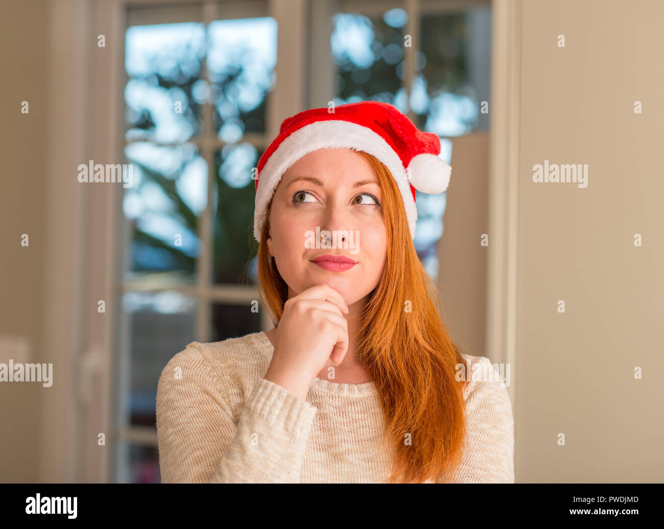 Redhead woman wearing santa claus hat serious face thinking about ...