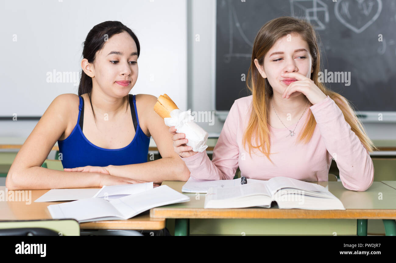 Two girls are eating sandwich at the desk and writing homework in the ...