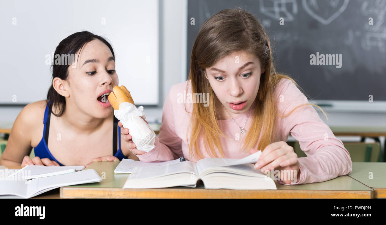 Two girls are eating sandwich at the desk and writing homework in the ...