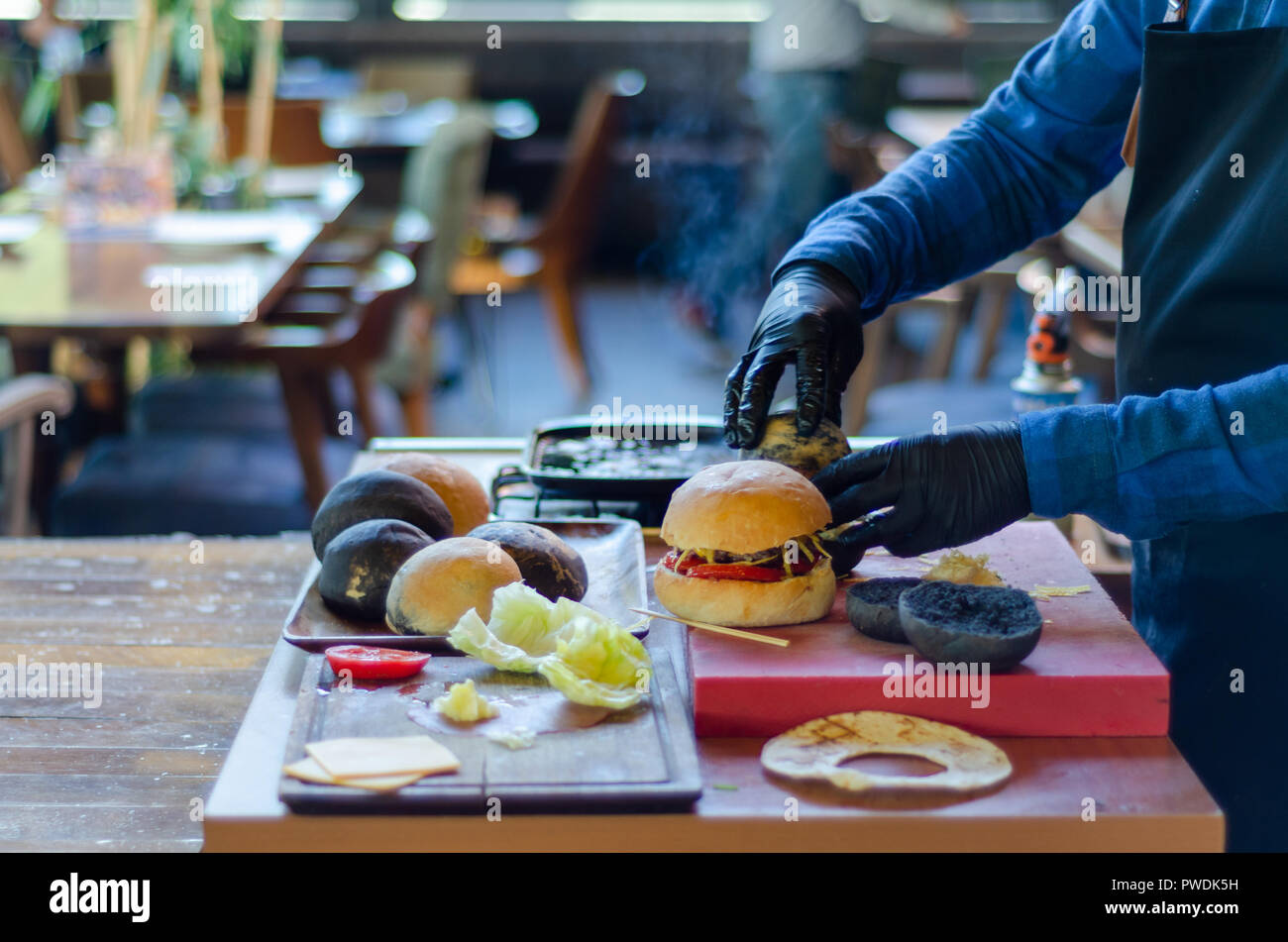 Chef is preparing a burger on the table in restaurant.He hands in black ...