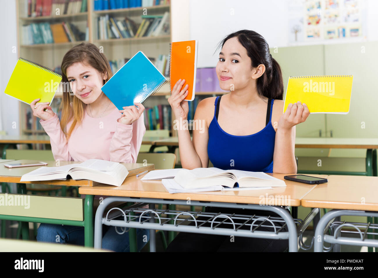 Portrait of two girl who are sitting with notebooks at the desk in the ...