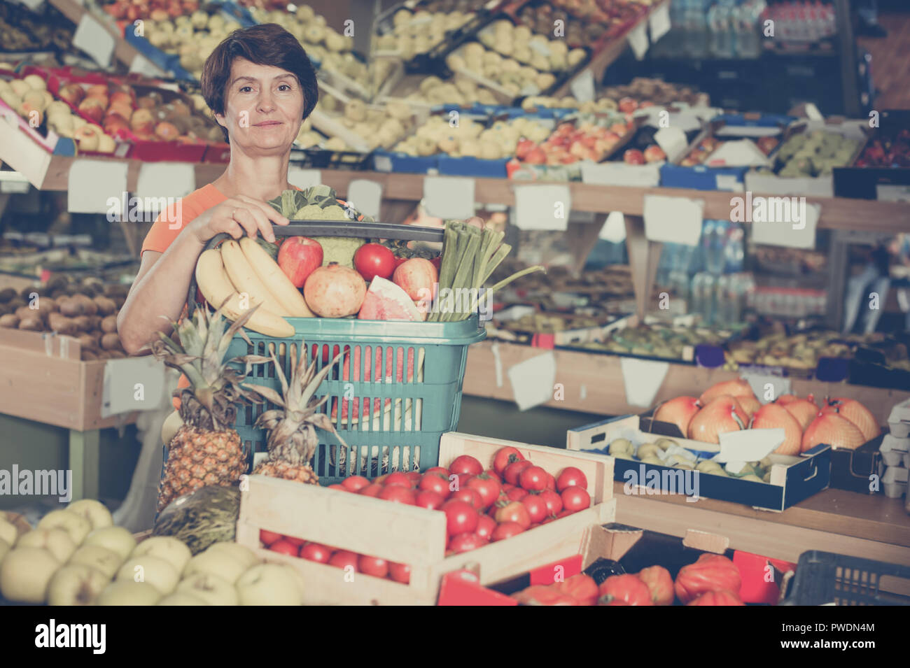 Glad woman is demonstraiting basket with variety goods in the fruit ...
