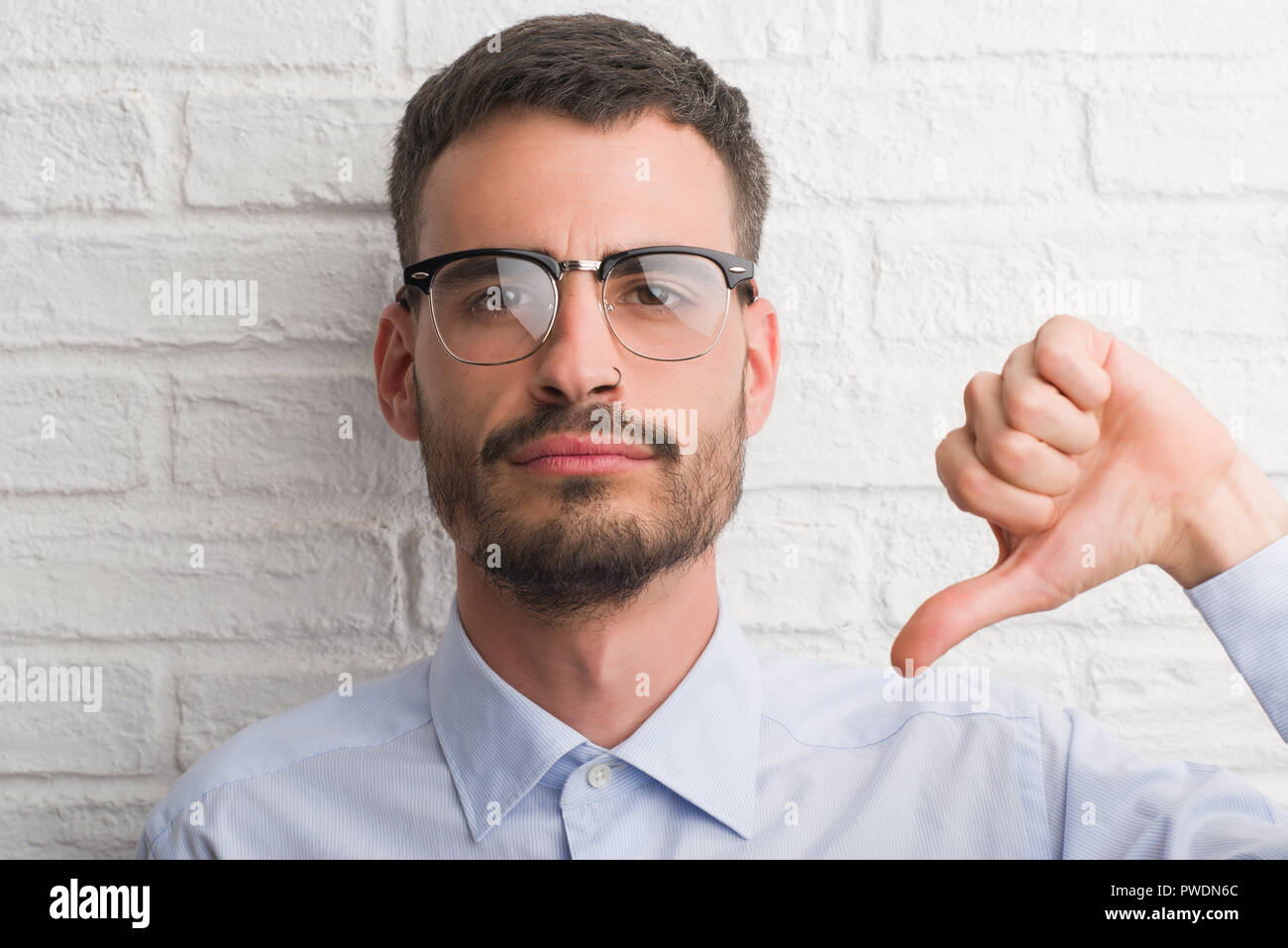 Young adult business man standing over white brick wall with angry face ...