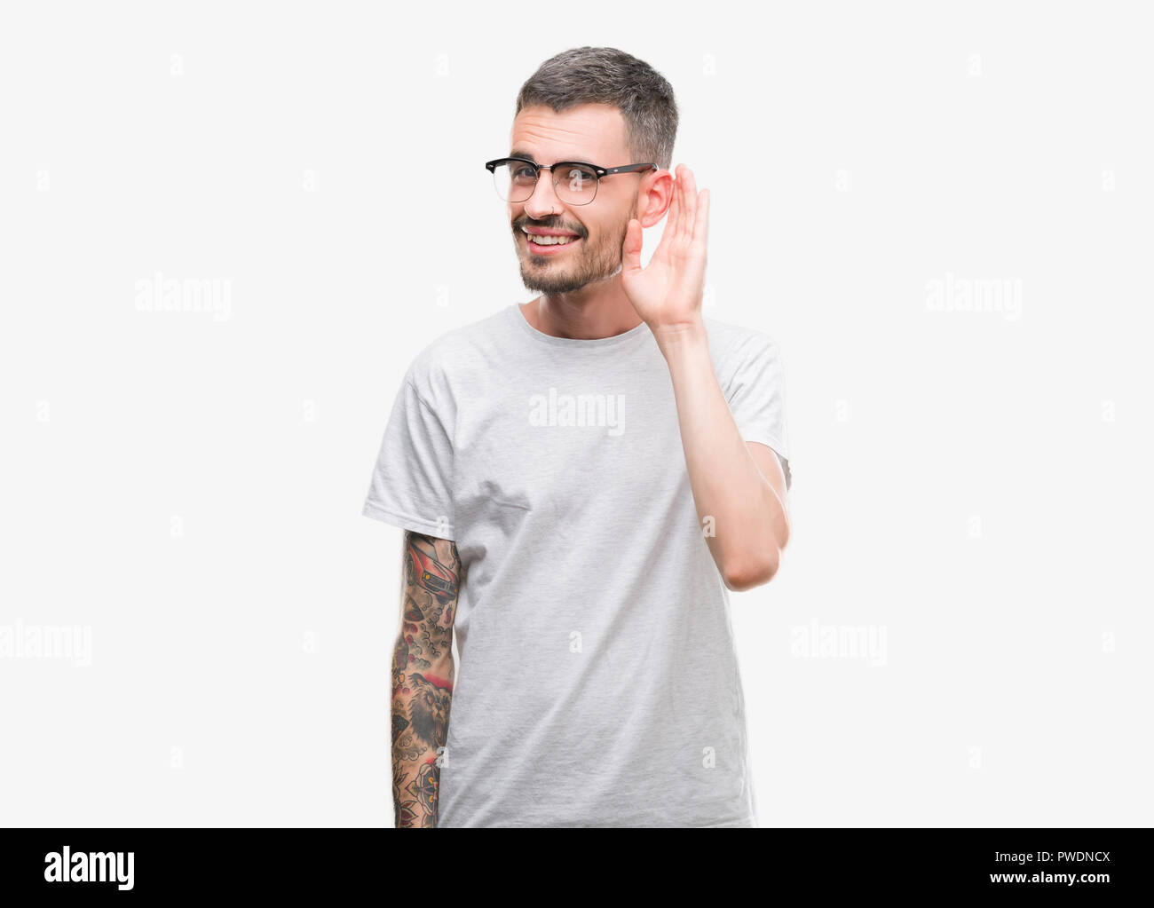 Young tattooed adult man smiling with hand over ear listening an ...