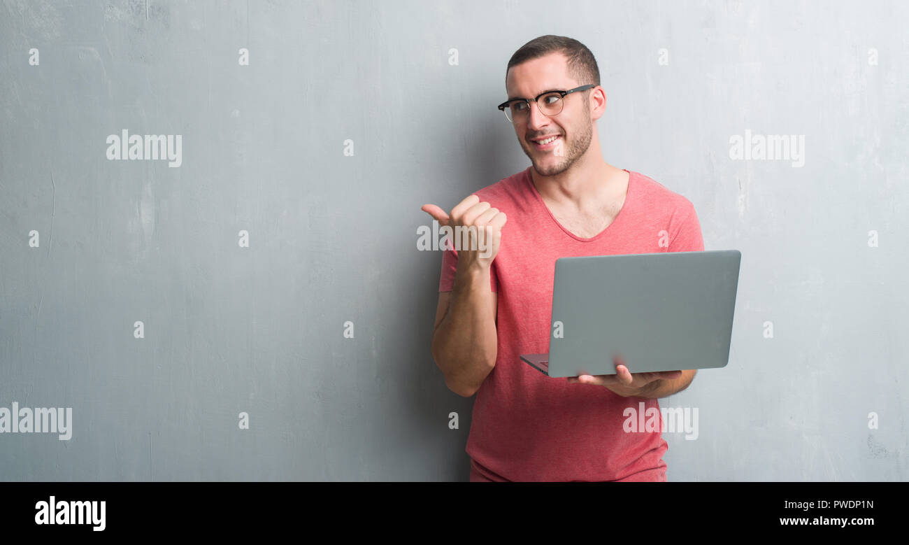 Young caucasian man over grey grunge wall using computer laptop ...