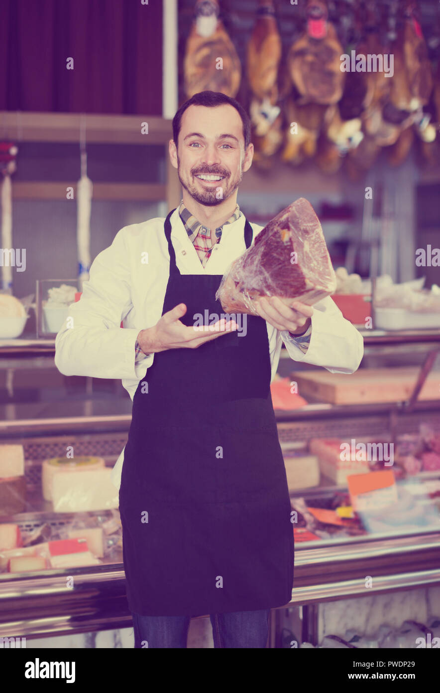 Positive man seller showing piece of meat in butcher’s shop Stock Photo ...