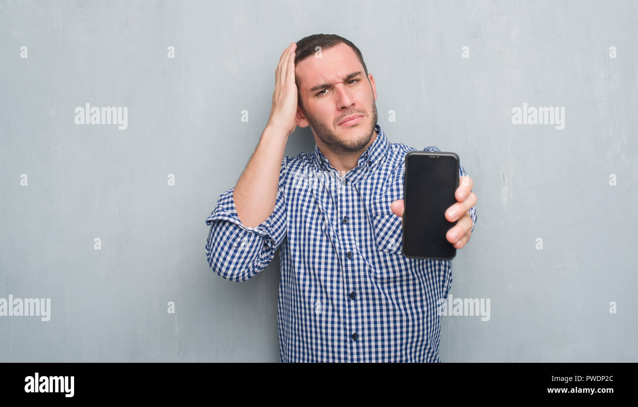Young caucasian man over grey grunge wall showing blank screen of ...