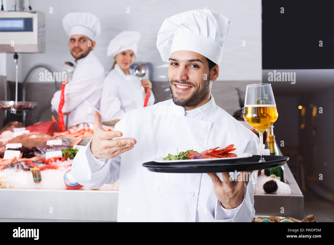 Handsome adult male chef with dishes on serving tray welcoming to fish ...