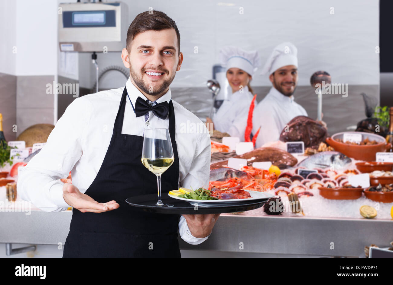 Portrait of positive waiter with serving tray offering dishes in fish ...