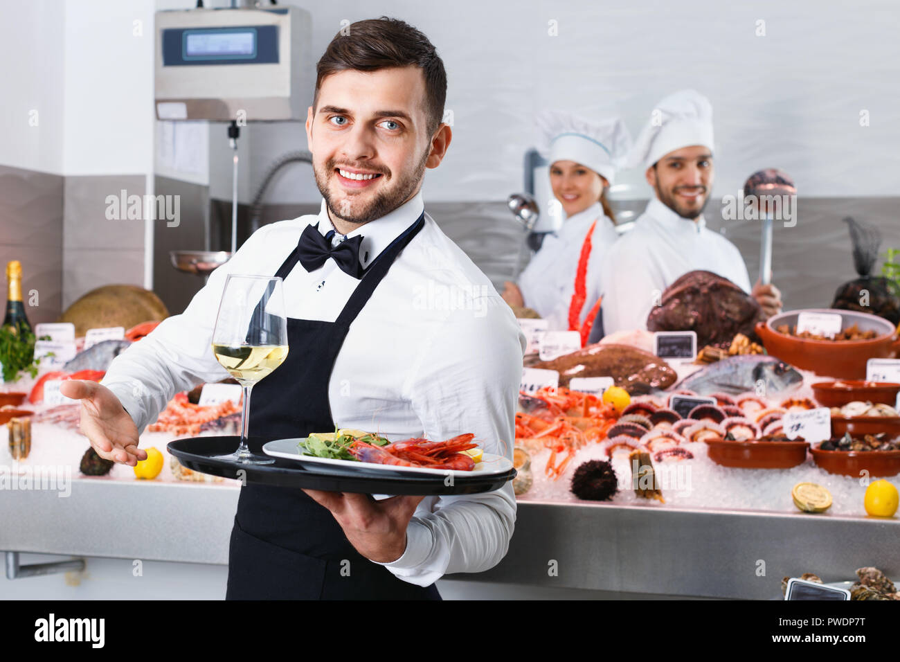 Glad positive smiling waiter holding tray with seafood dishes at fish ...