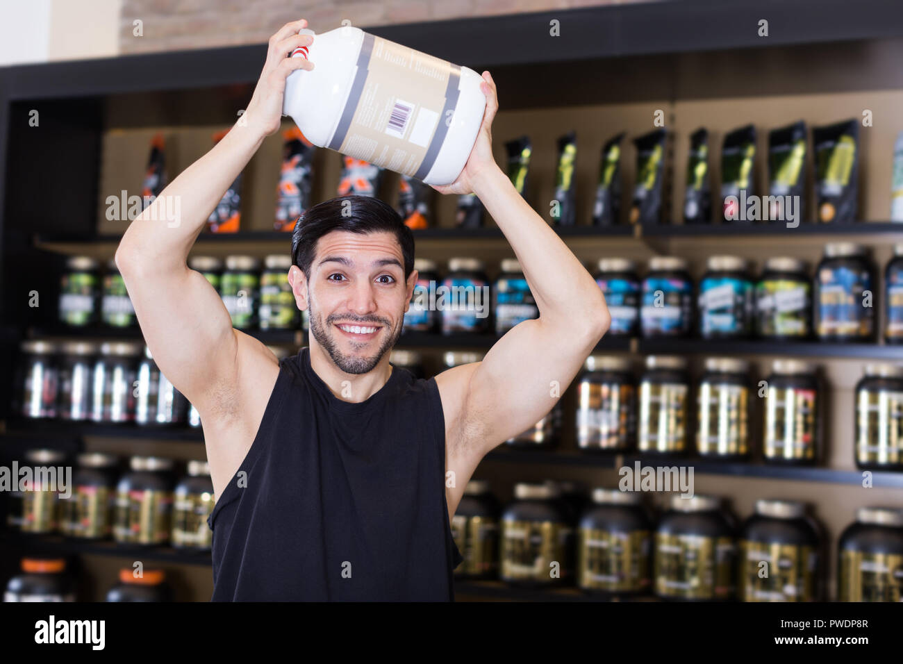 Young bodybuilder holding big pot of sport supplements over head in ...