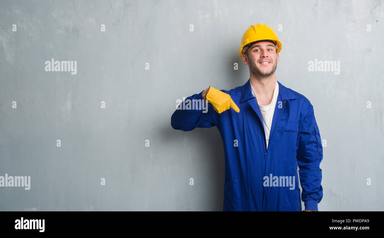 Young caucasian man over grey grunge wall wearing contractor uniform ...