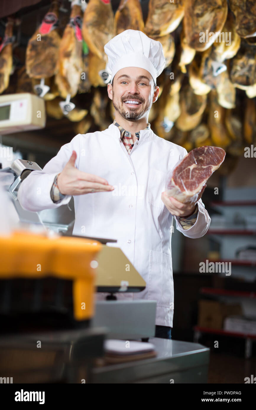 Smiling man butcher showing piece of meat in butcher’s store Stock ...