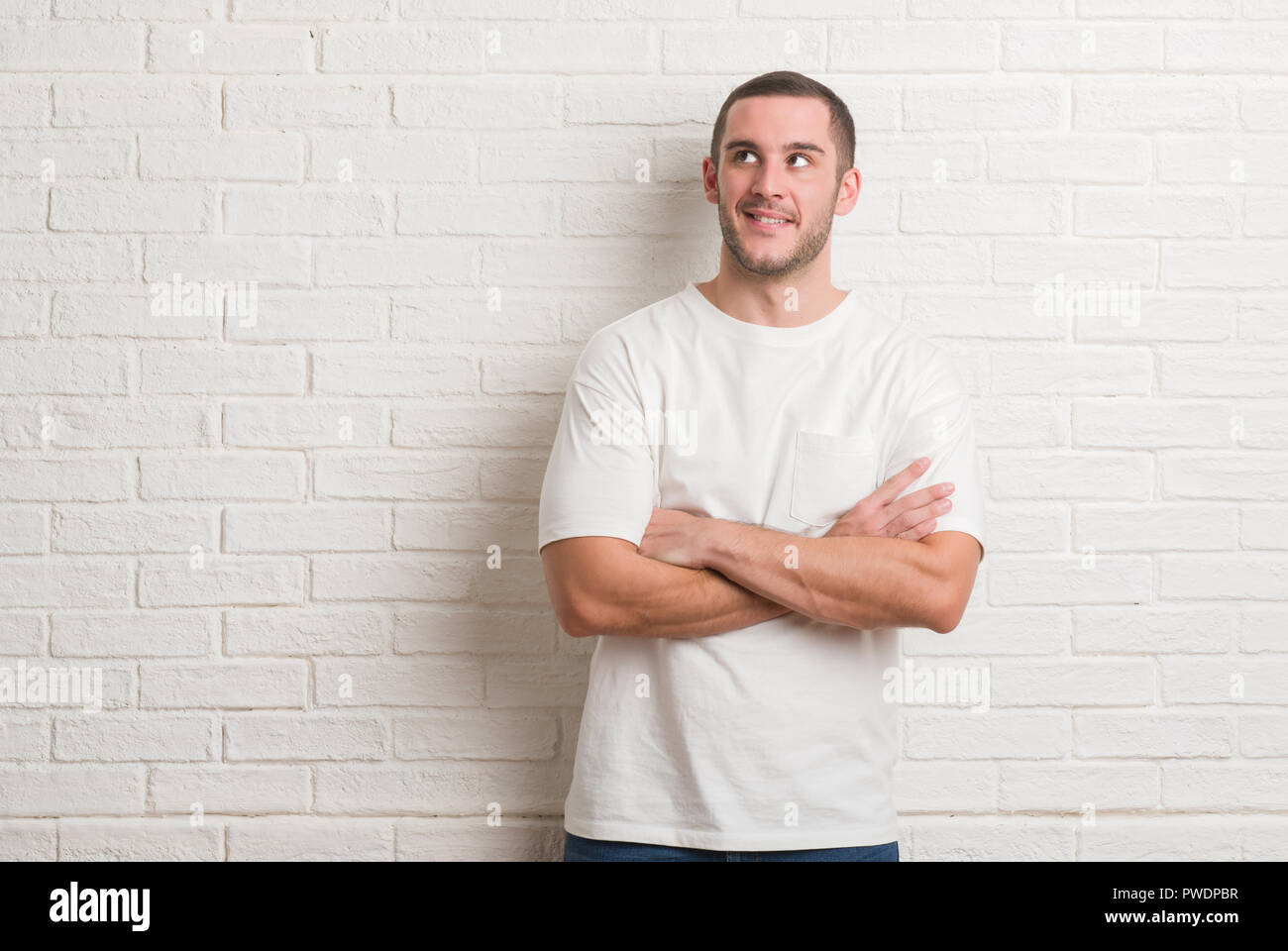 Young caucasian man standing over white brick wall smiling looking side ...