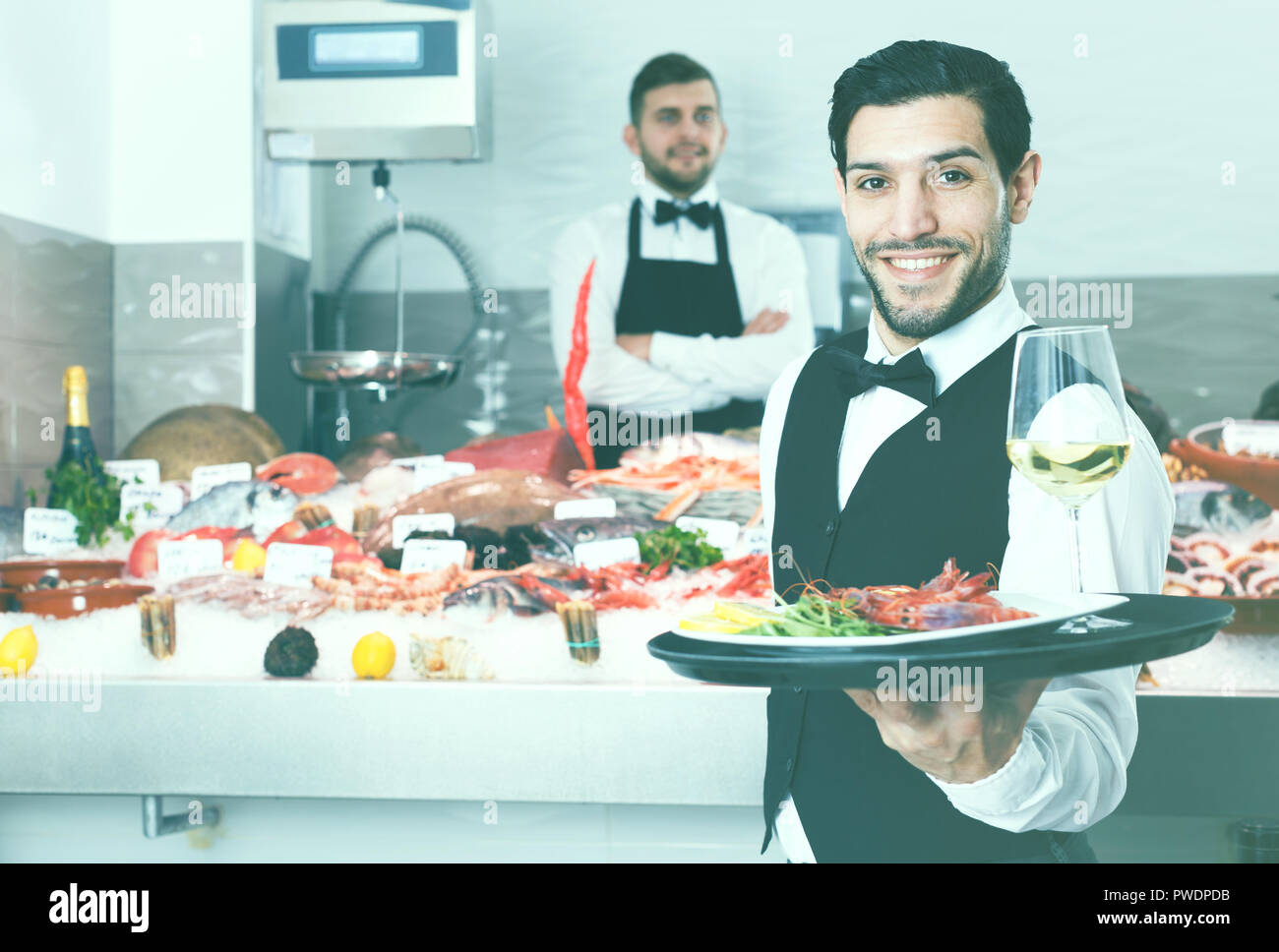 Portrait of smiling waiter with serving tray offering dishes in fish ...