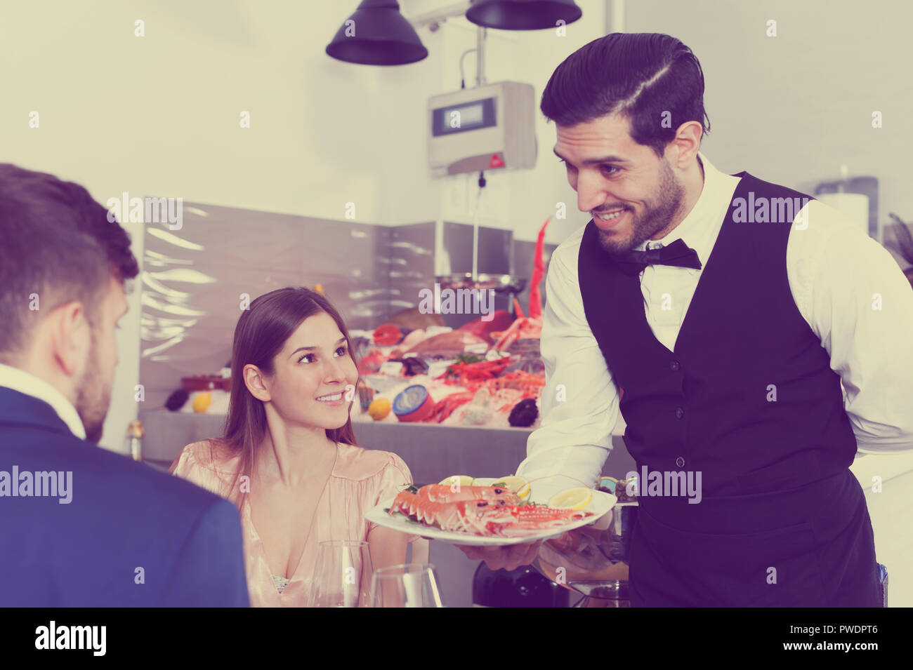 Positive waiter showing seafood meals to visitors of fish restaurant ...