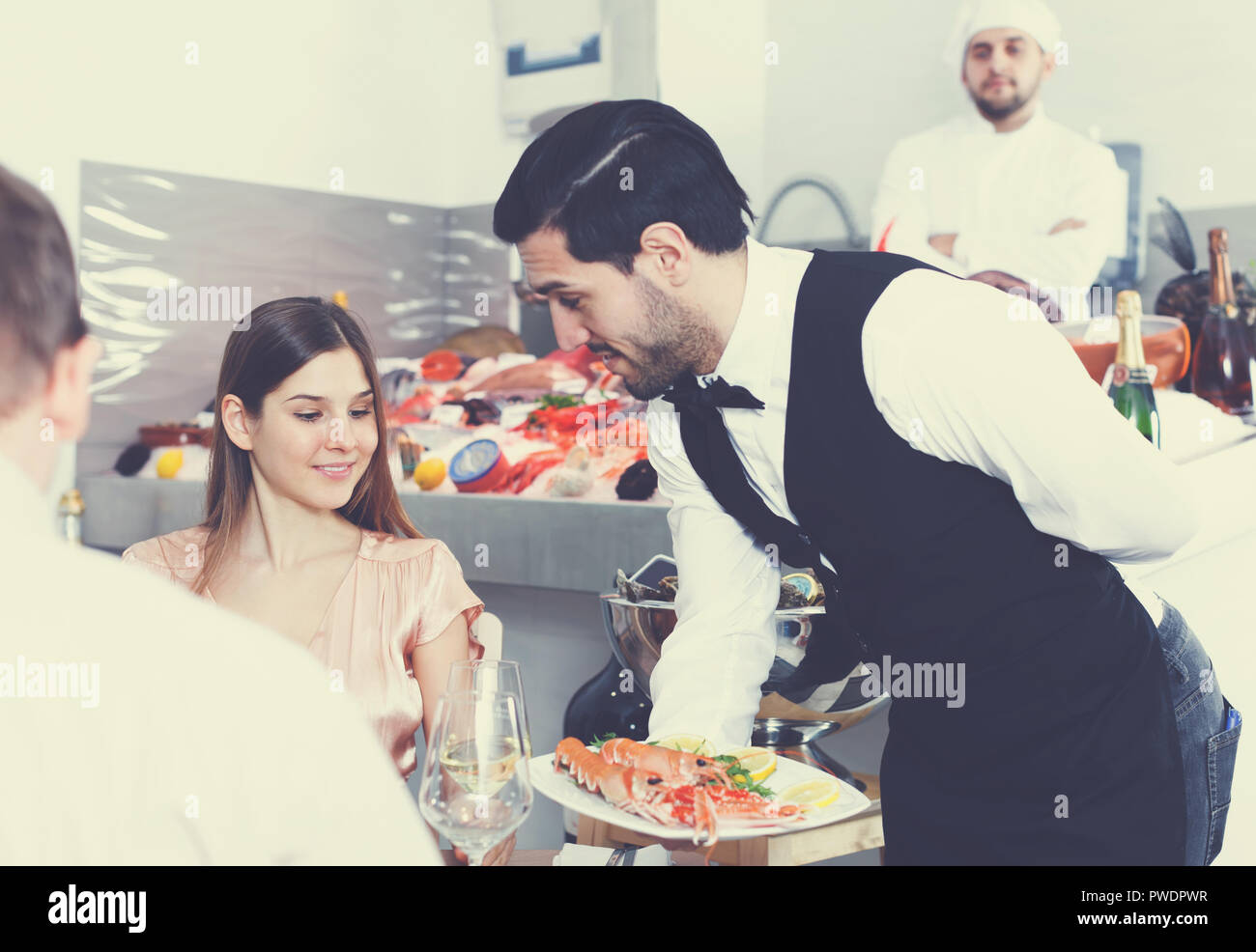 Positive restaurant waiter serving seafood meals to visitors Stock ...